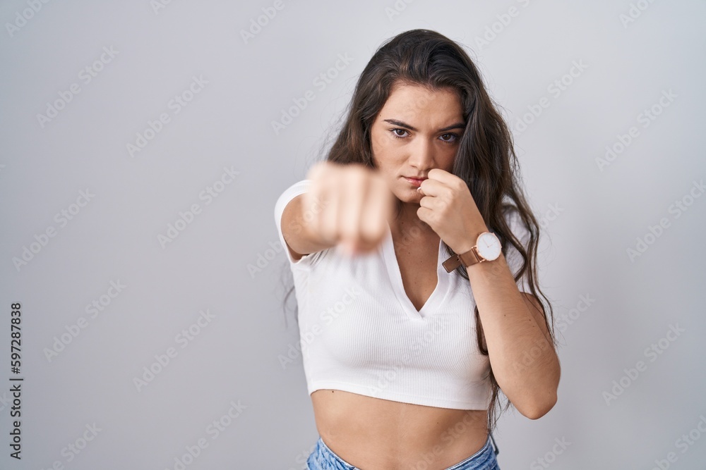 Young teenager girl standing over white background punching fist to ...