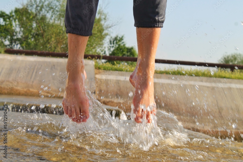 Feet of a young man barefoot in the water on a concrete slab. Side sun ...
