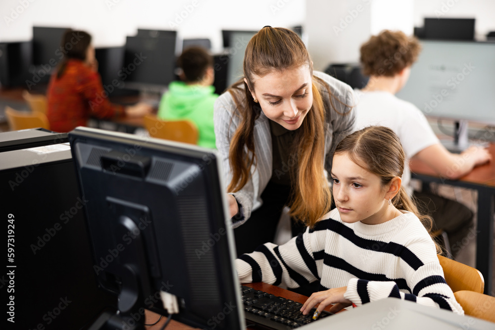 Female teacher and her student, young girl, looking at monitor of PC ...
