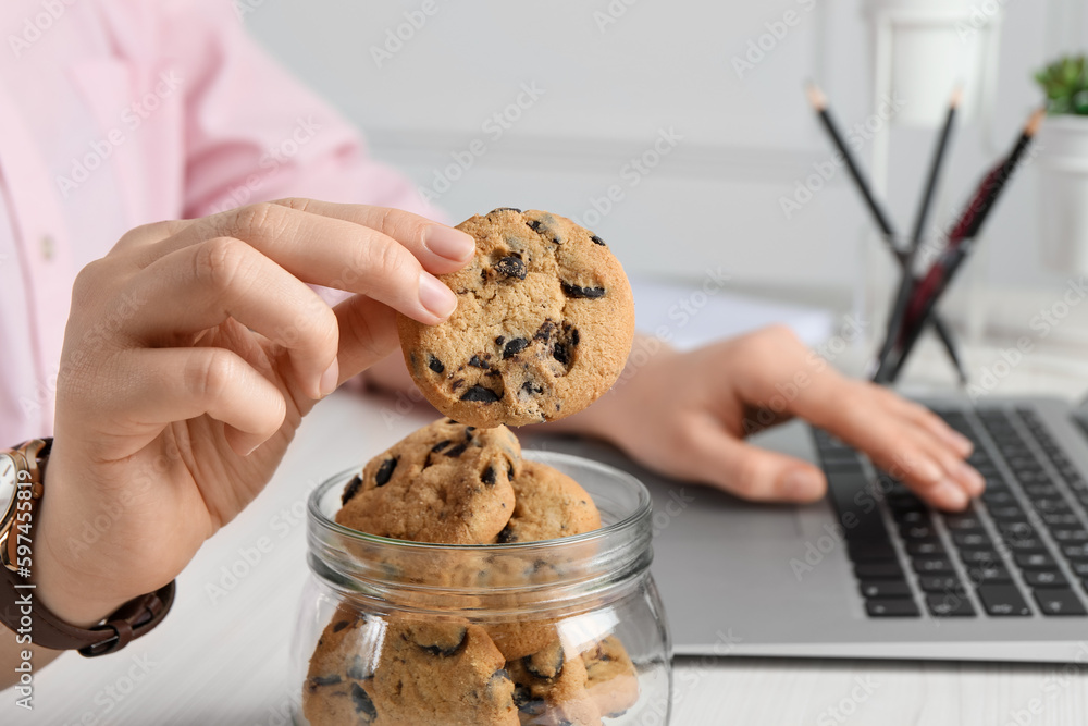 Office worker taking chocolate chip cookie from jar at workplace ...