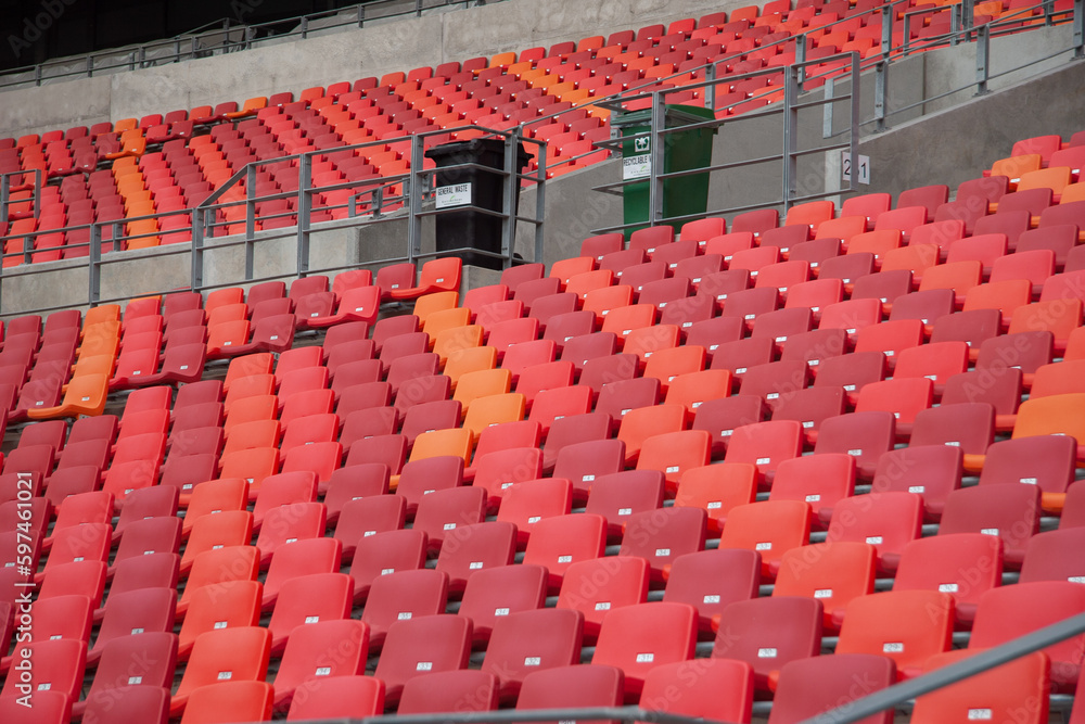 Staggered rows of empty red stadium seats, with refuse bins on landing ...