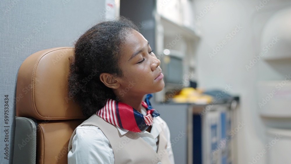 Woman african american stewardess, flight attendant sitting on seat in airplane looking tired ...
