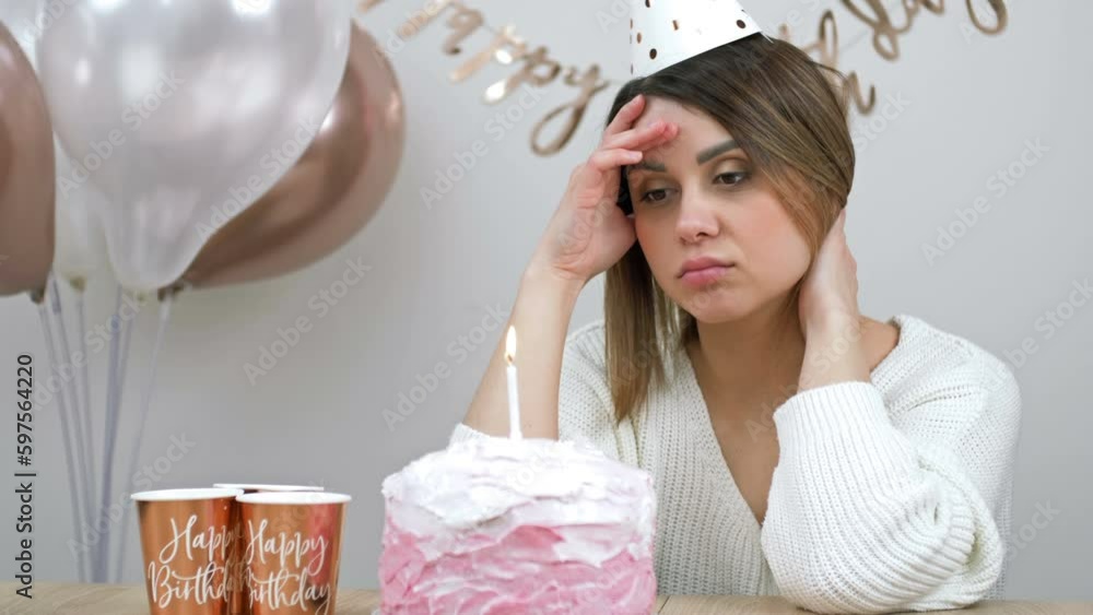 Sad birthday. Beautiful girl sits alone in front of a birthday cake ...