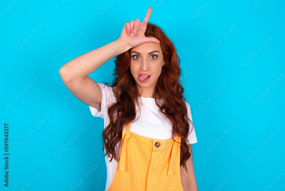 Young redhead woman wearing orange overall over blue background ...