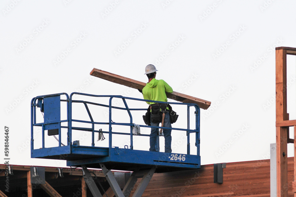 A worker using a scissor lift carries a beam on to the rooftop of a ...