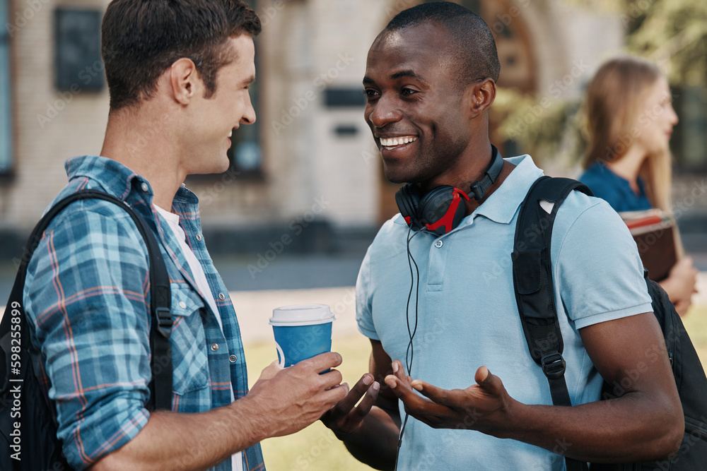Two happy young men talking while standing against University building ...