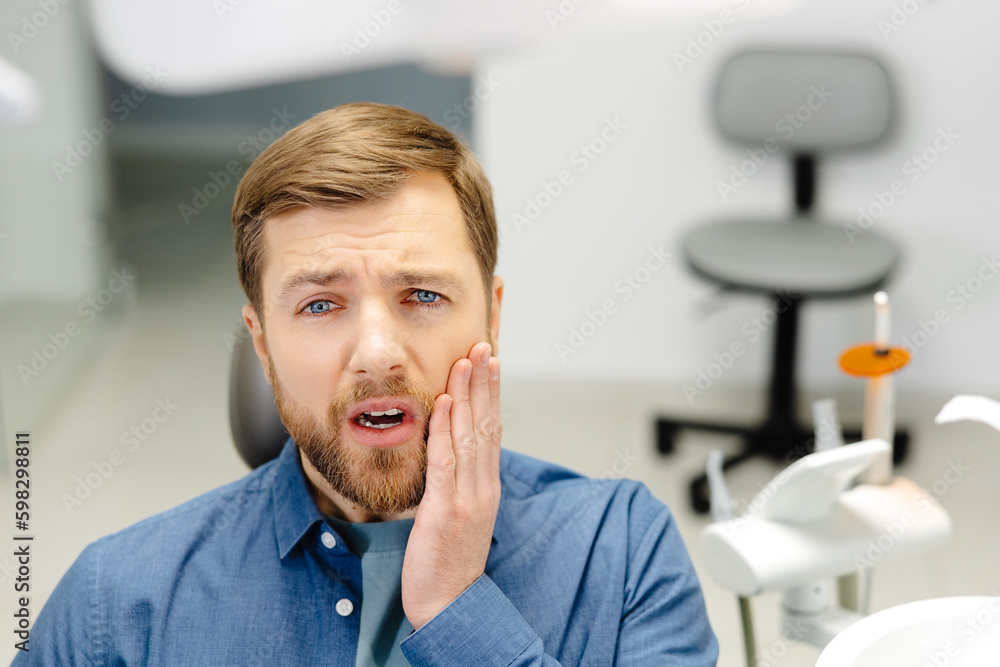 Sad man sitting in dental chair suffering from acute tooth pain ...