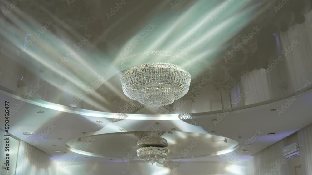Light of crossed rotating white spotlights on multi level ceiling with ...