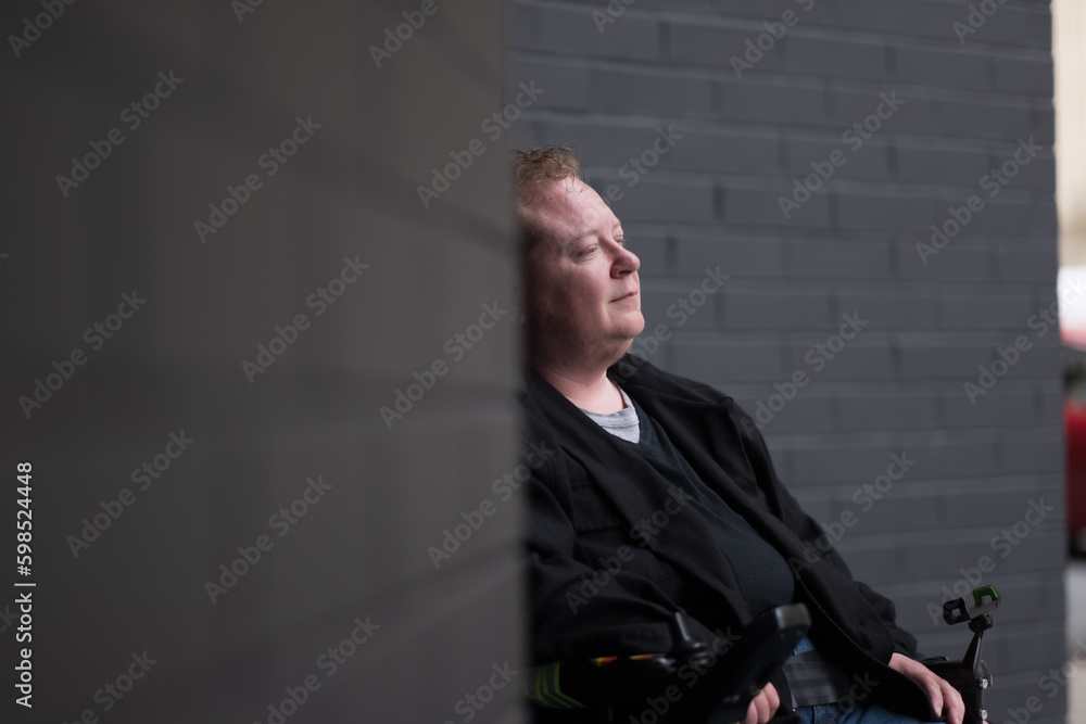 Sitting in his powerchair with a black brick wall in the background, a ...
