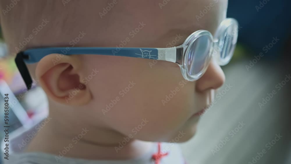 One year old infant with glasses is watching TV at home. White ...