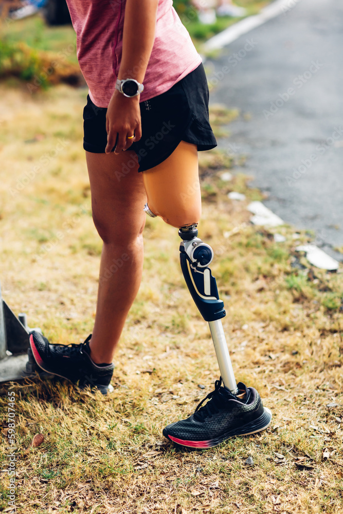 Athlete with prosthetic leg doing warm up exercise on park. Woman ...