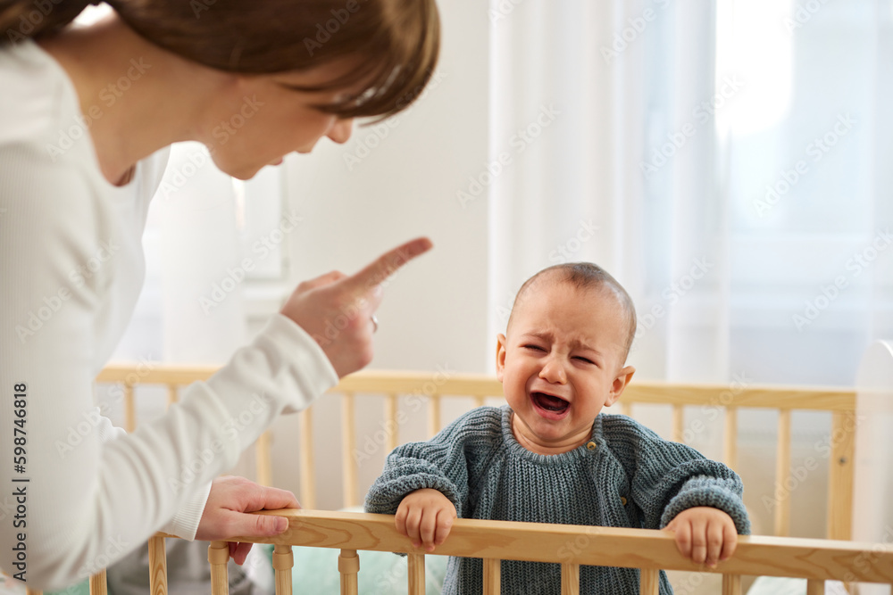 Little baby boy crying in the crib while his mother pointing finger and ...