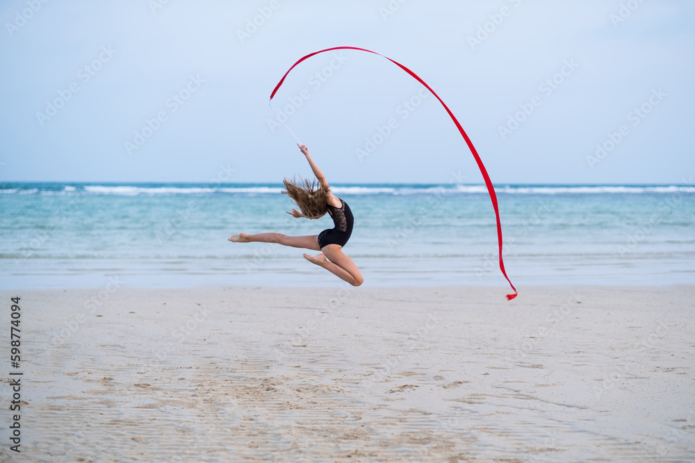 girl gymnast makes an element with a ribbon on the beach, rhythmic ...