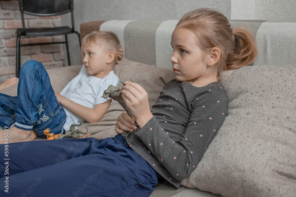 Little brother and sister watch TV together sitting on the sofa in the ...