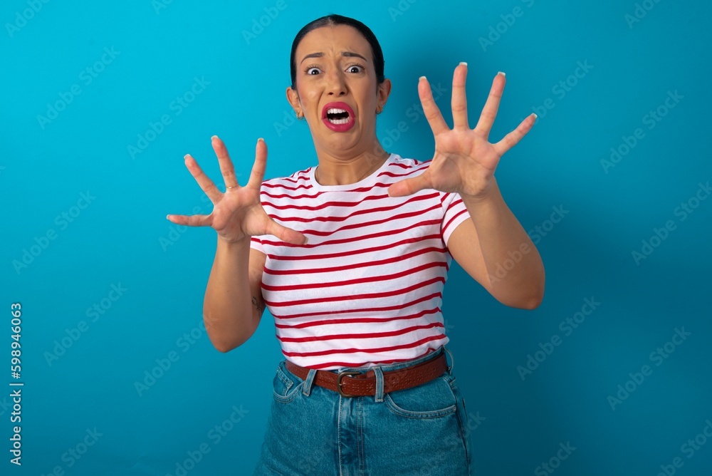 Dissatisfied beautiful woman wearing striped T-shirt over blue studio ...