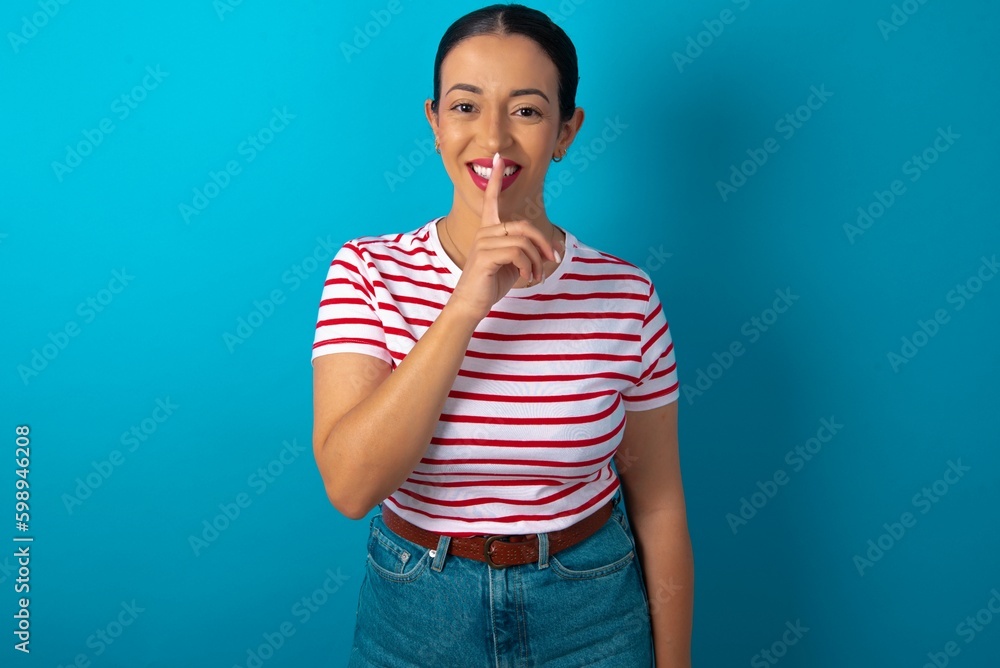 Smiling beautiful woman wearing striped T-shirt over blue studio ...