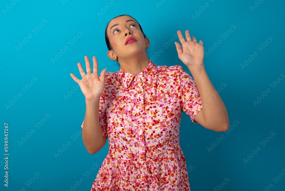 beautiful woman wearing floral dress over blue studio background keeps ...