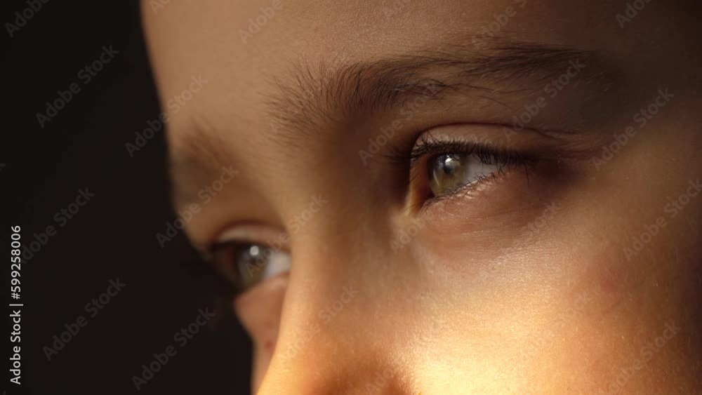 Close-up of the kid eyes. A dreaming boy looks in the dark, a ray of ...