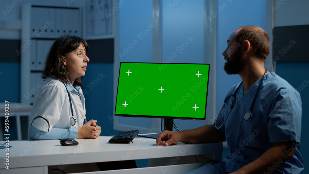 Medic and assistant looking at computer monitor with green screen ...