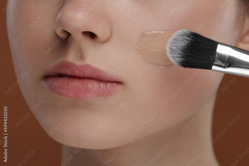 Teenage girl applying foundation on face with brush against brown ...