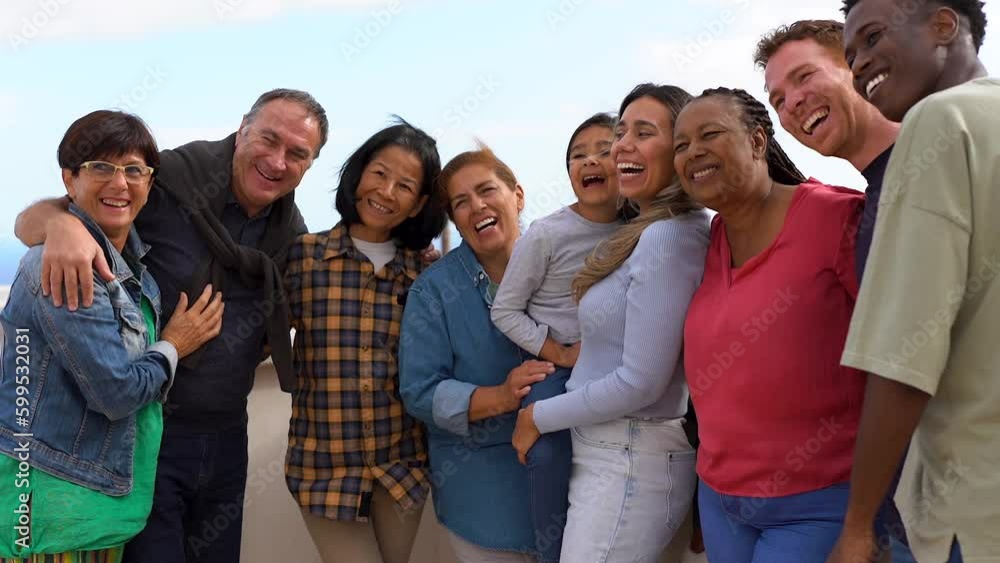 Group of multigenerational people hugging each other while smiling in front of camera ...