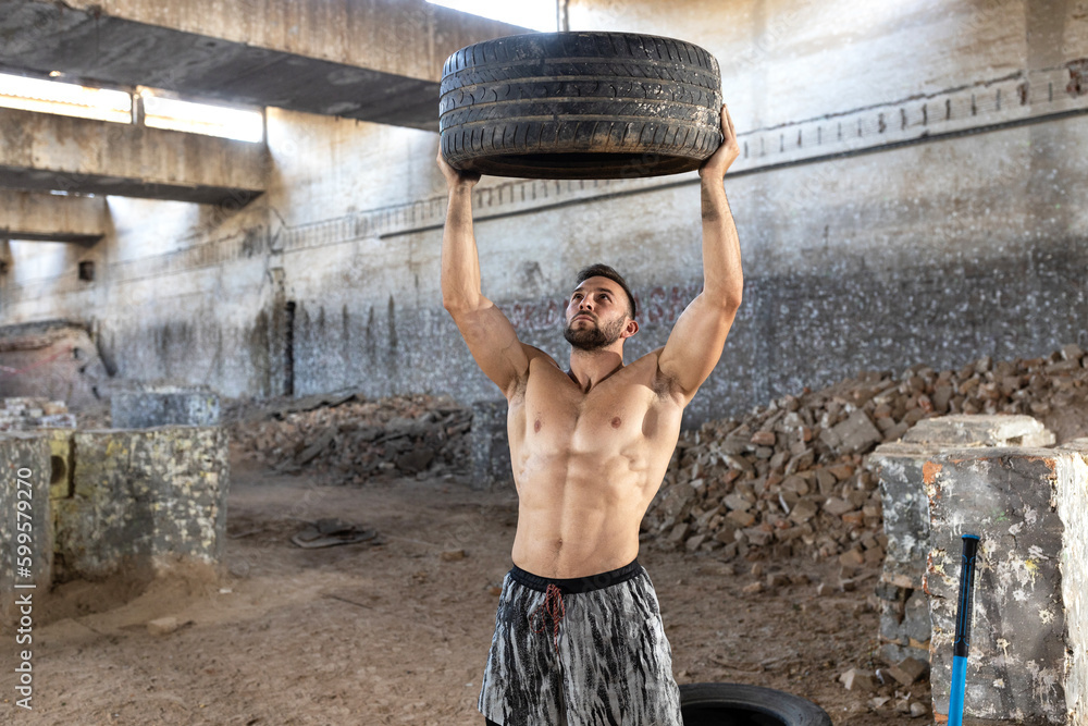 Strong ripped handsome man lifted a car tire above his head during ...
