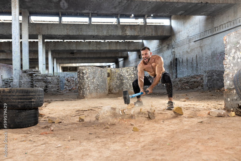 Strong handsome man waving a hammer in squatting position and breaking ...