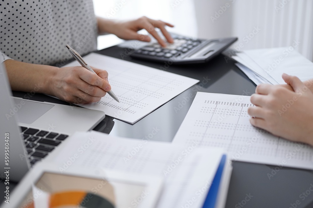Woman accountant using a calculator and laptop computer while counting ...