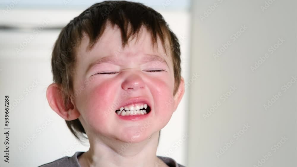 Portrait of a crying toddler baby in gray clothes on the background of ...