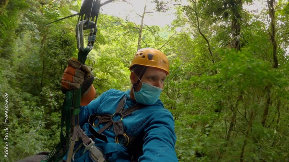 Adventurous man on a fast zipline descent through lush treetops in ...