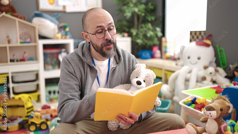 Young bald man preschool teacher reading story book at kindergarten ...