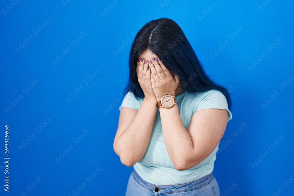 Young modern girl with blue hair standing over blue background with sad ...