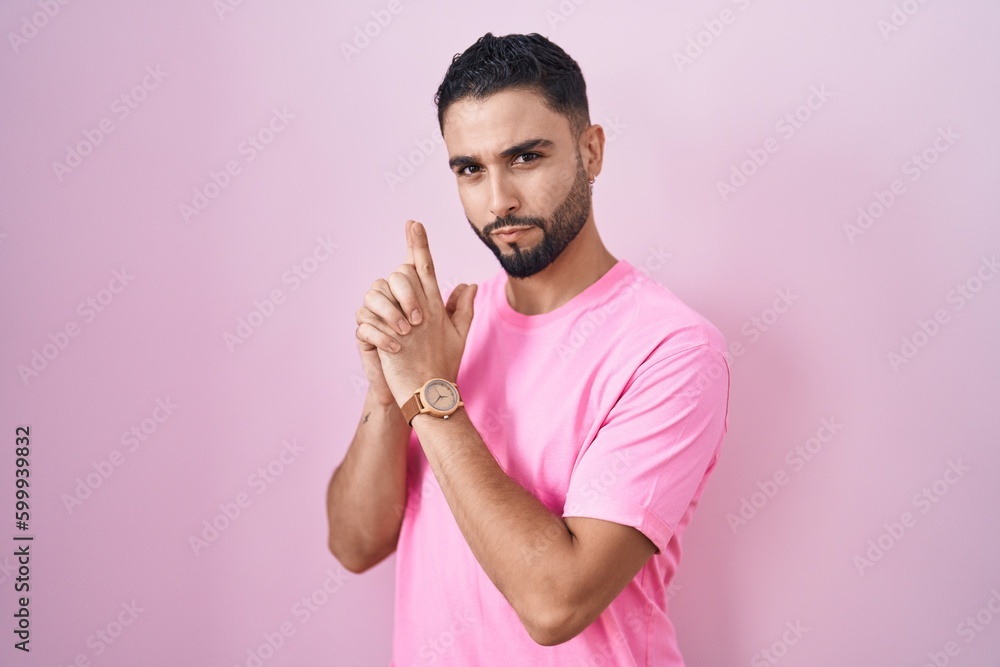 Hispanic young man standing over pink background holding symbolic gun ...
