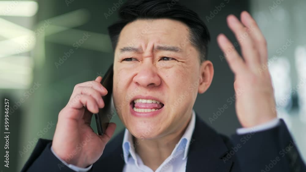 Close up. Angry asian man in formal suit arguing while talking on ...