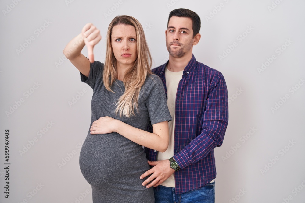 Young couple expecting a baby standing over white background looking ...