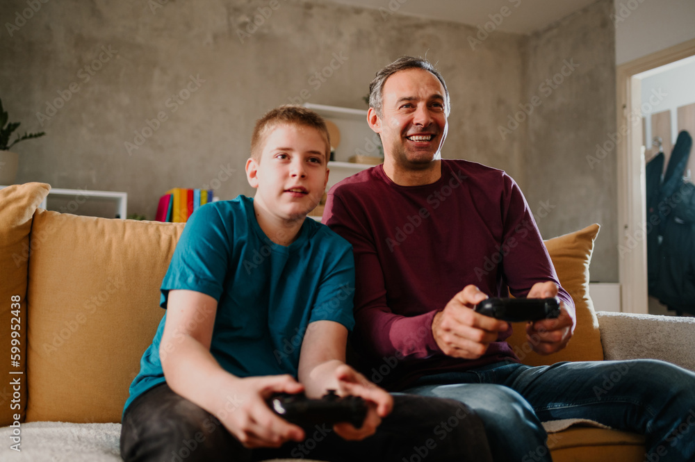 Middle aged father and his teenage son enjoying while playing video ...