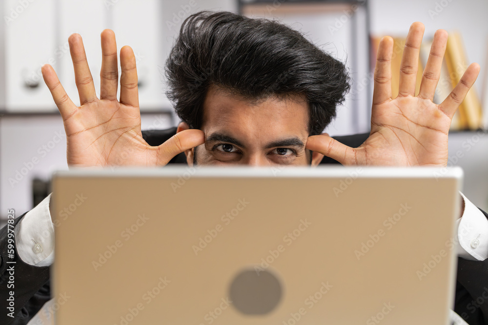 Indian businessman hiding behind laptop computer, making funny face ...