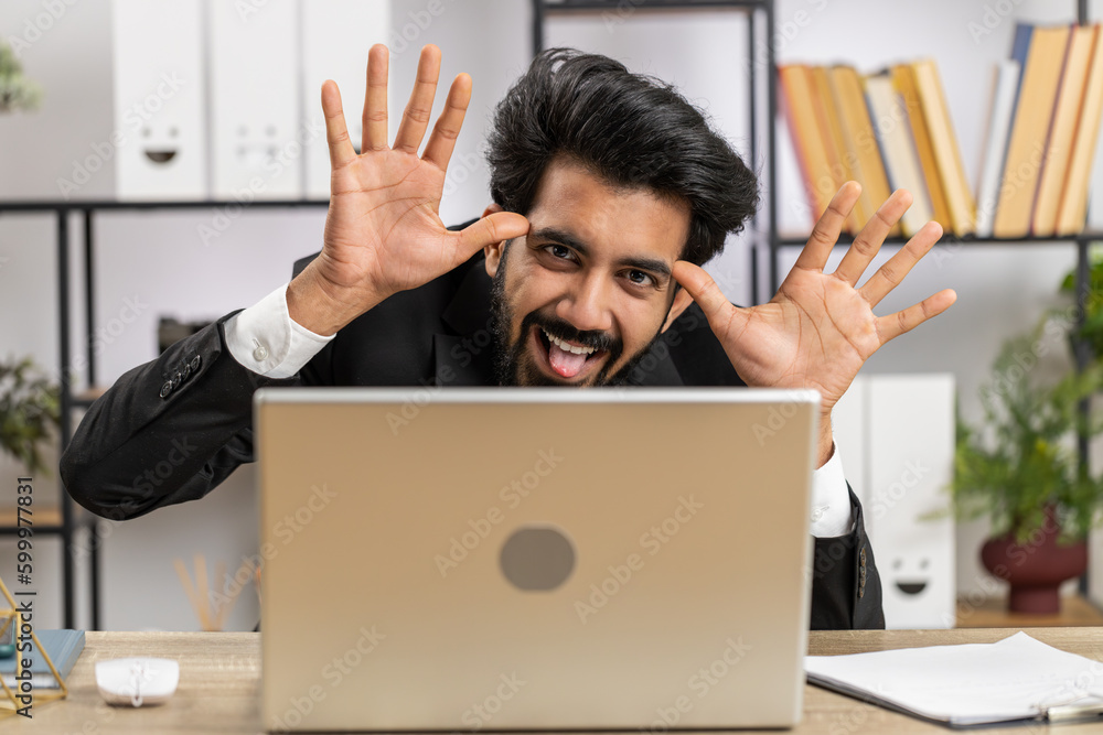 Indian businessman hiding behind laptop computer, making funny face ...