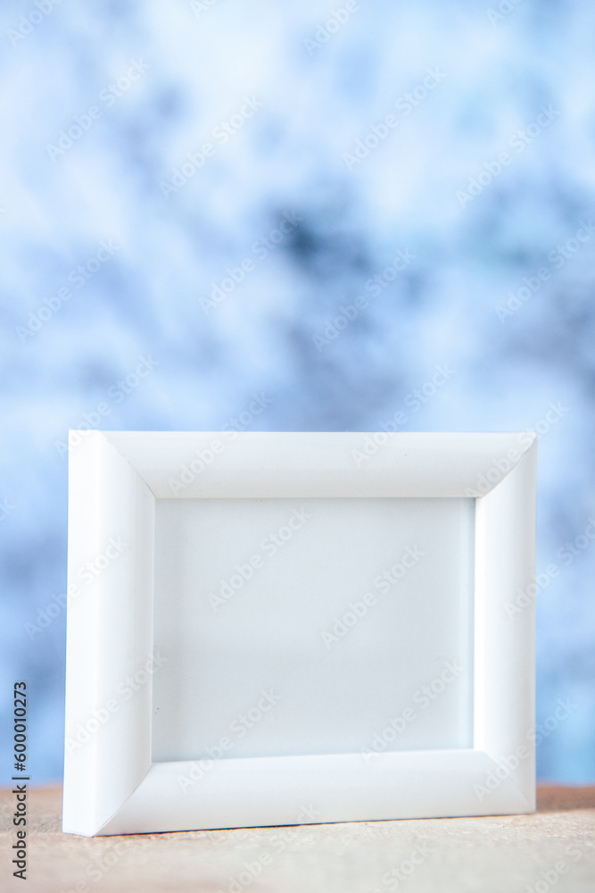 Vertical view of white empty picture frame standing on table on light ...