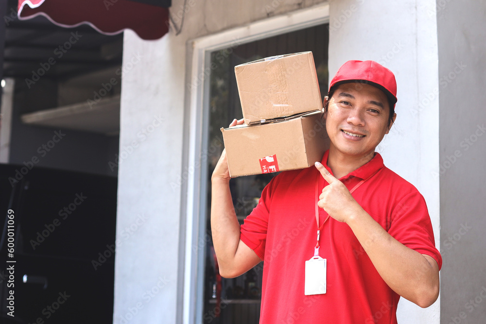 Smiling deliveryman in red uniform carrying pile of packages on ...