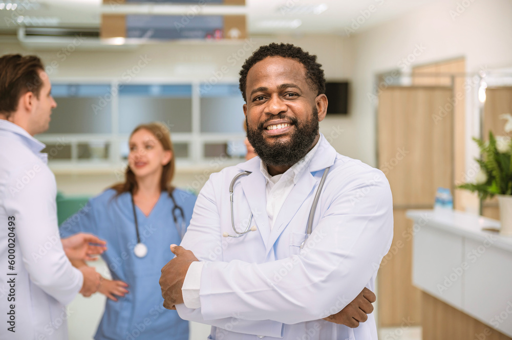 doctor smiles at camera with his arms crossed and medical team ...