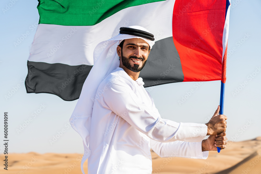 Middle-eastern emirati man wearing arab kandura holding emirati flag in ...