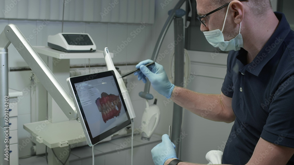 A professional dentist man looks at a 3d model of teeth on a computer ...