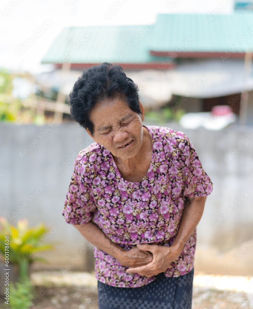 Fototapeta An old Asian woman holding her stomach with her hands ... Fototapeta An old Asian woman holding her stomach with her hands ...