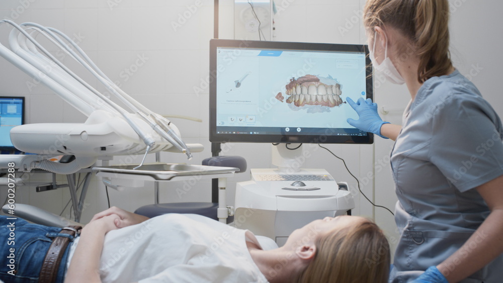 Girl doctor dentist demonstrates a 3D model of teeth on a touch monitor ...