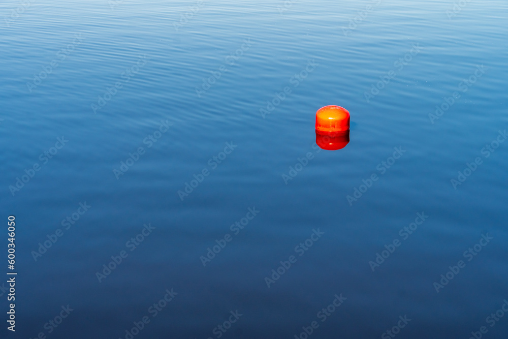 Red anchor buoy in cylinder shape lies on a calm sea surface. Water ...
