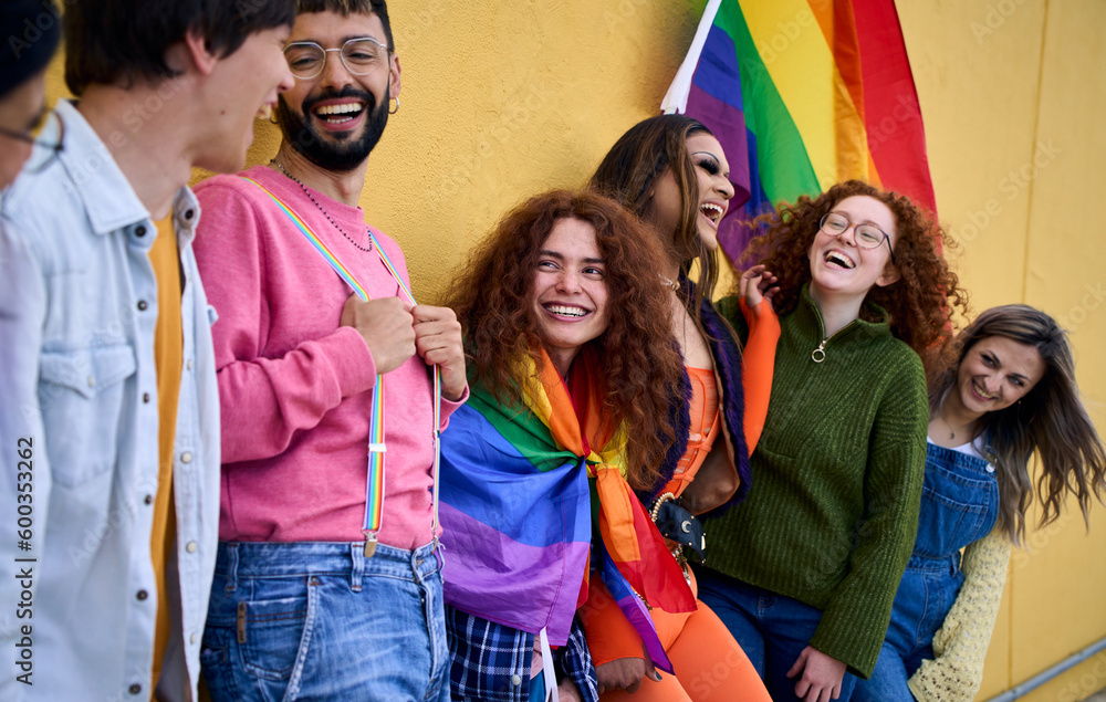 Portrait of group laughing young friends standing on wall yellow. LGBT ...