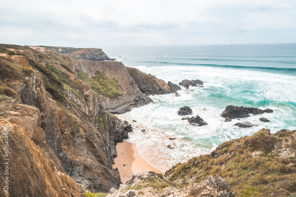Steep cliffs plunging into the yellow-orange sand watered by the waves ...
