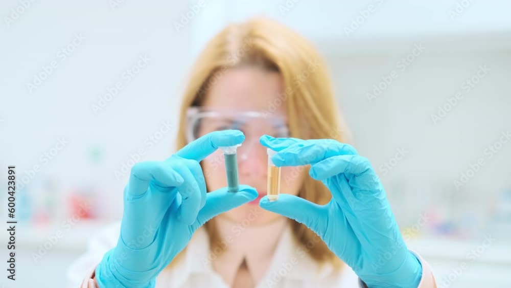 Scientist in rubber gloves shakes test tubes with blue and yellow ...