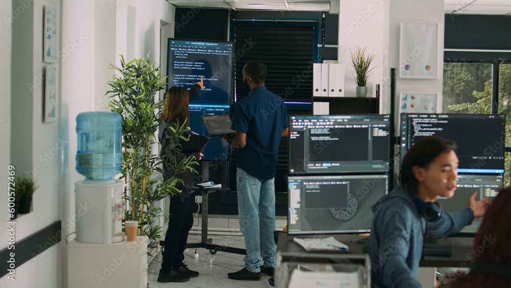 Diverse Team Of System Developers Analyzing Code On Big Tv Screen Checking Errors In Artificial
